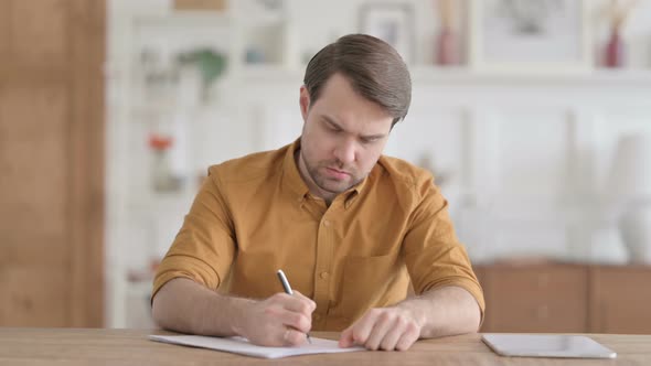 Young Man Thinking while Writing on Paper in Office, Stock Footage